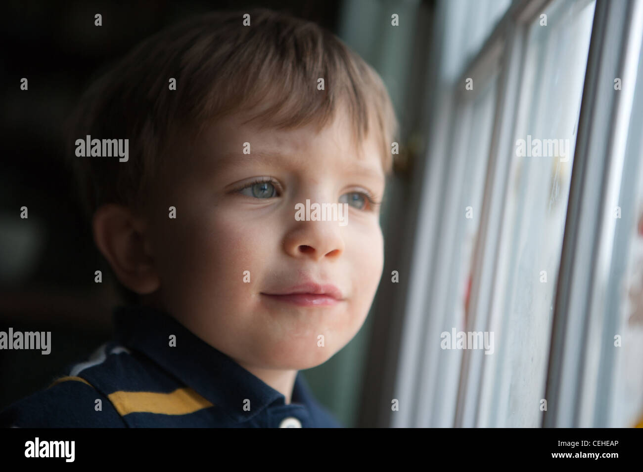 close up of a two year old boy looking out the window, with serious ...