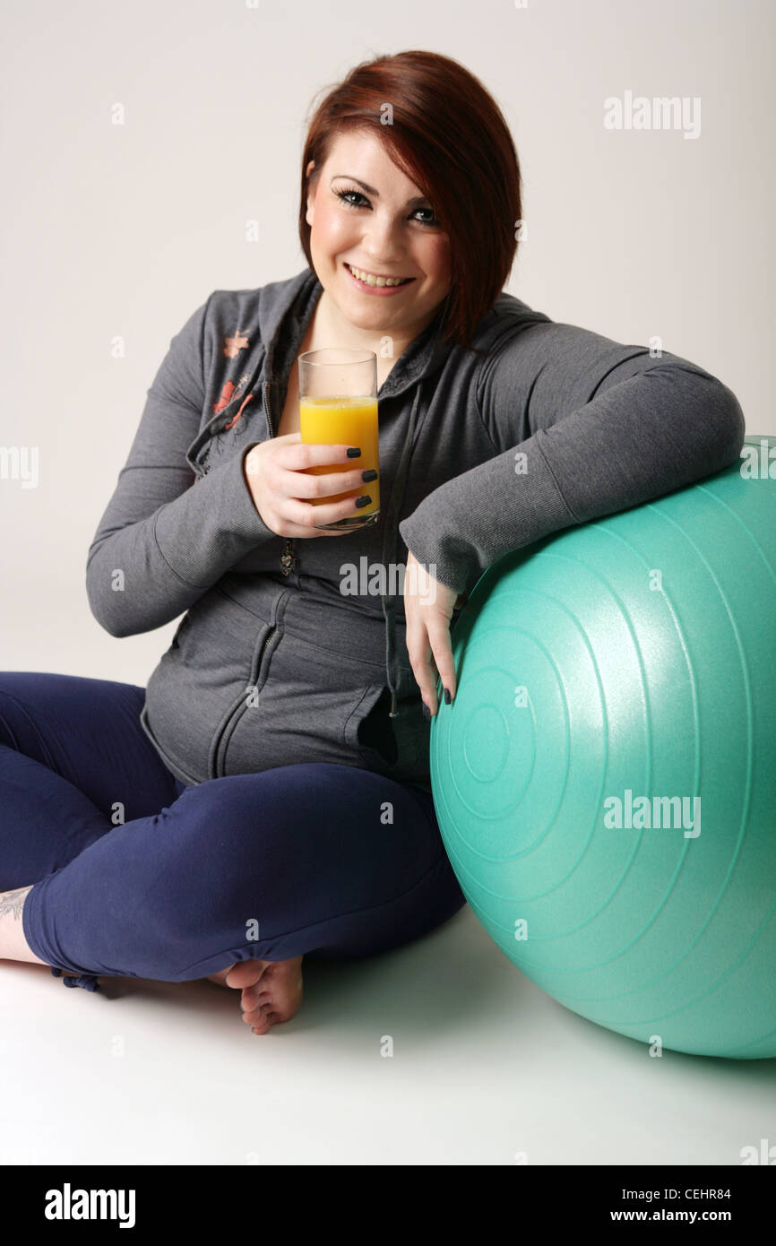 Woman resting arm on exercise ball and holding a glass of orange juice ...