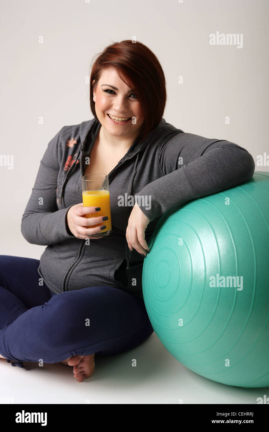 Woman resting arm on exercise ball and holding a glass of orange juice ...