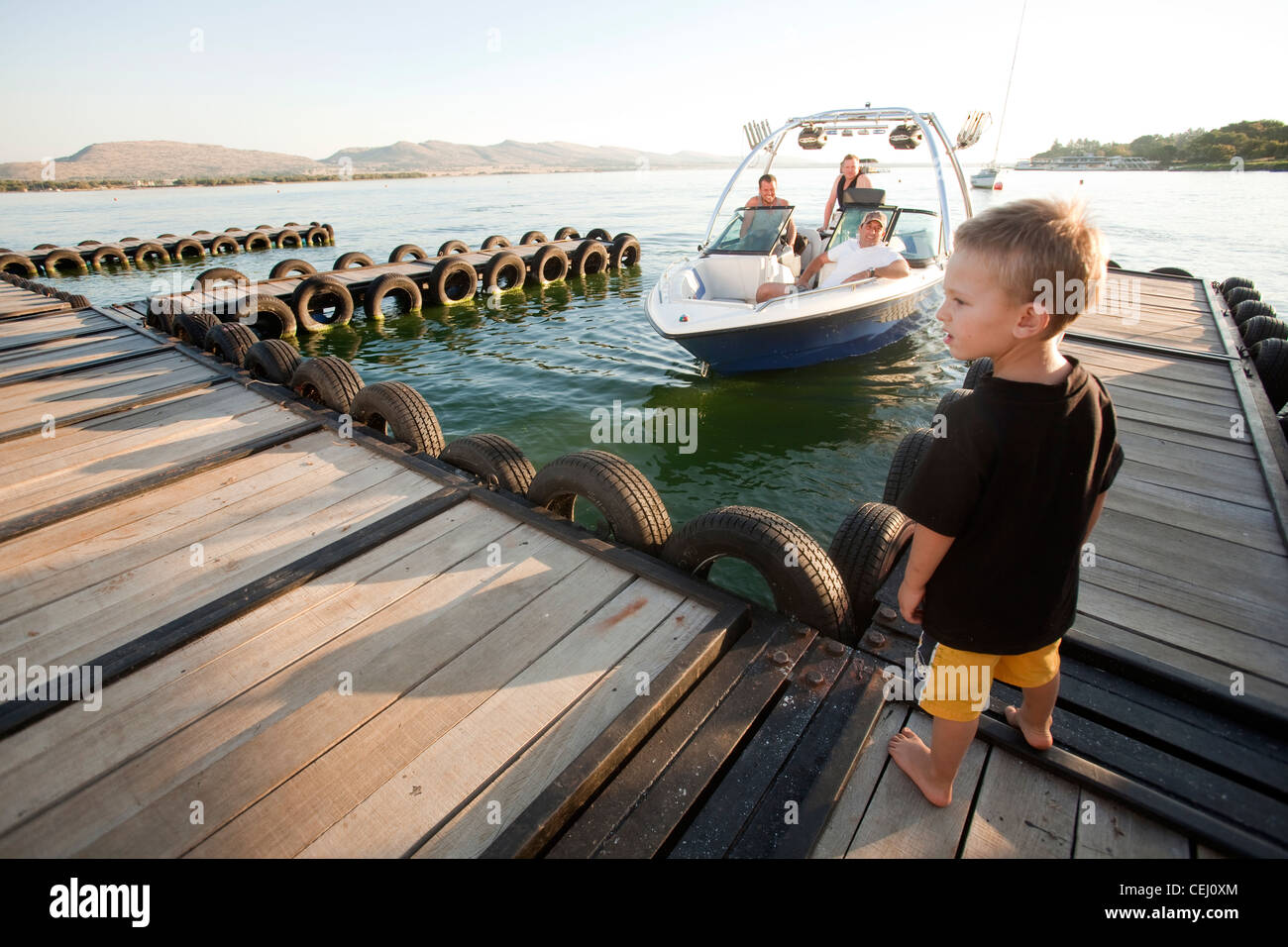 Boy standing on jetty with boat in background,Hartebeestpoort Dam,North ...