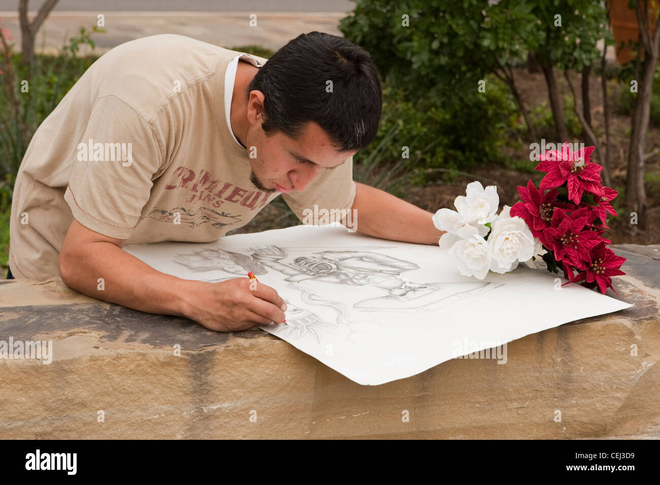 Young Hispanic male artist works on pencil drawing at an outdoor plaza ...
