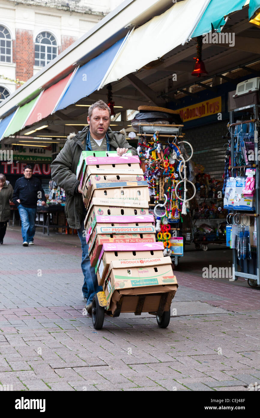 Market trader wheels a stack of fruit and vegetable boxes in Leicester ...