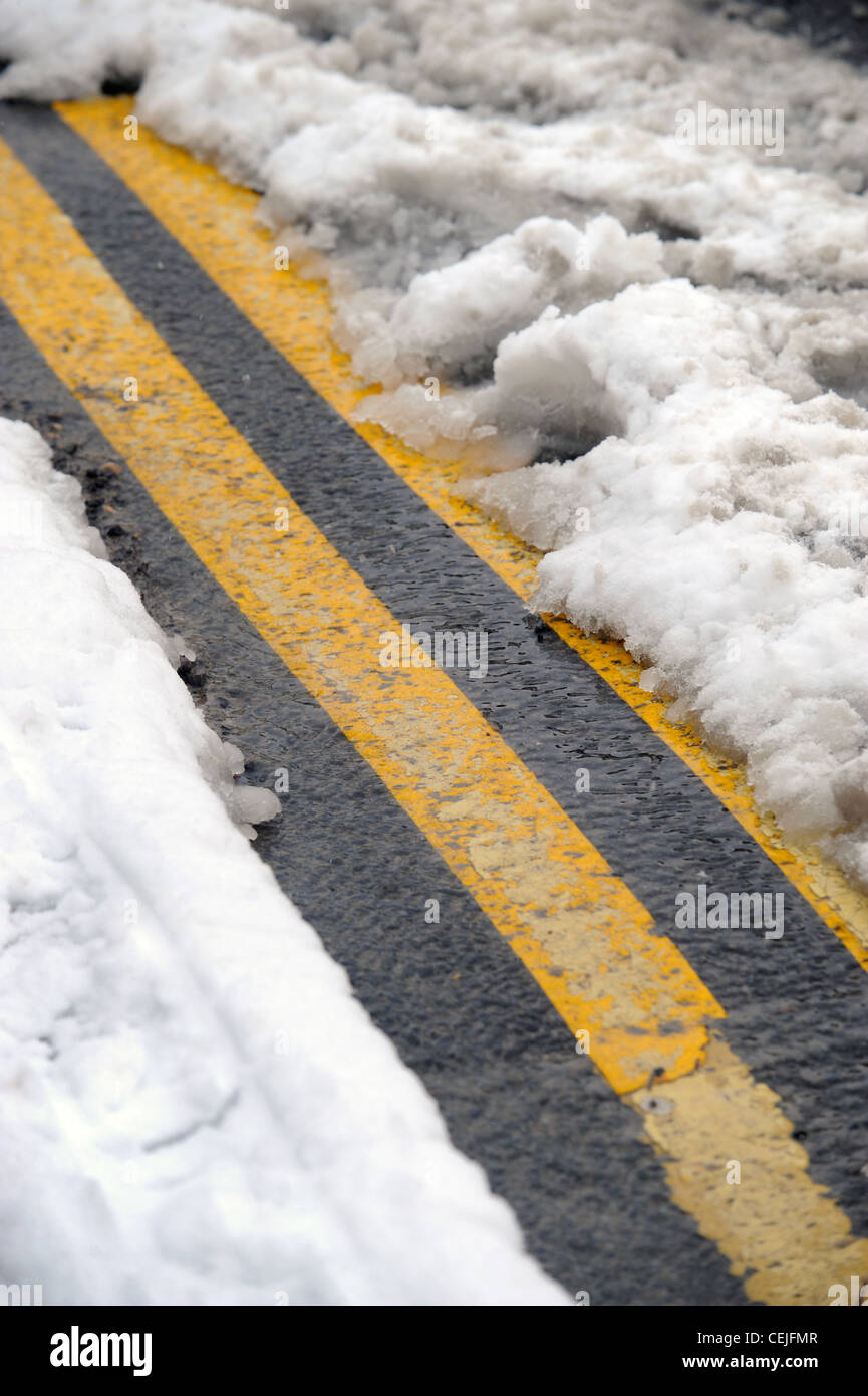 A double yellow line road marking emerges from under thawing snow UK ...