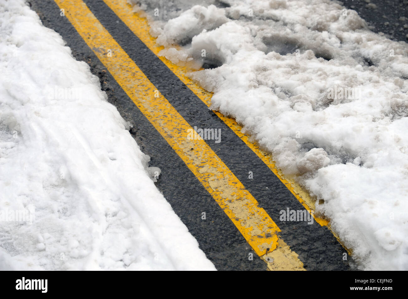A double yellow line road marking emerges from under thawing snow UK ...