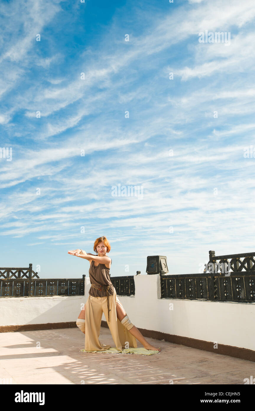 Beautiful young dancer performing yoga-dance outdoors with blue sky and ...