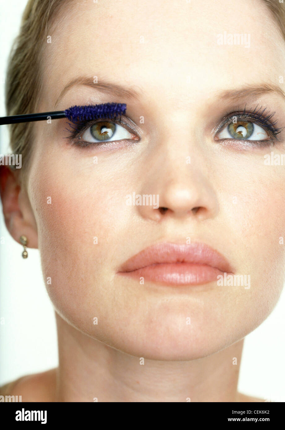 Close up image of female's face, applying purple mascara, unsmiling ...