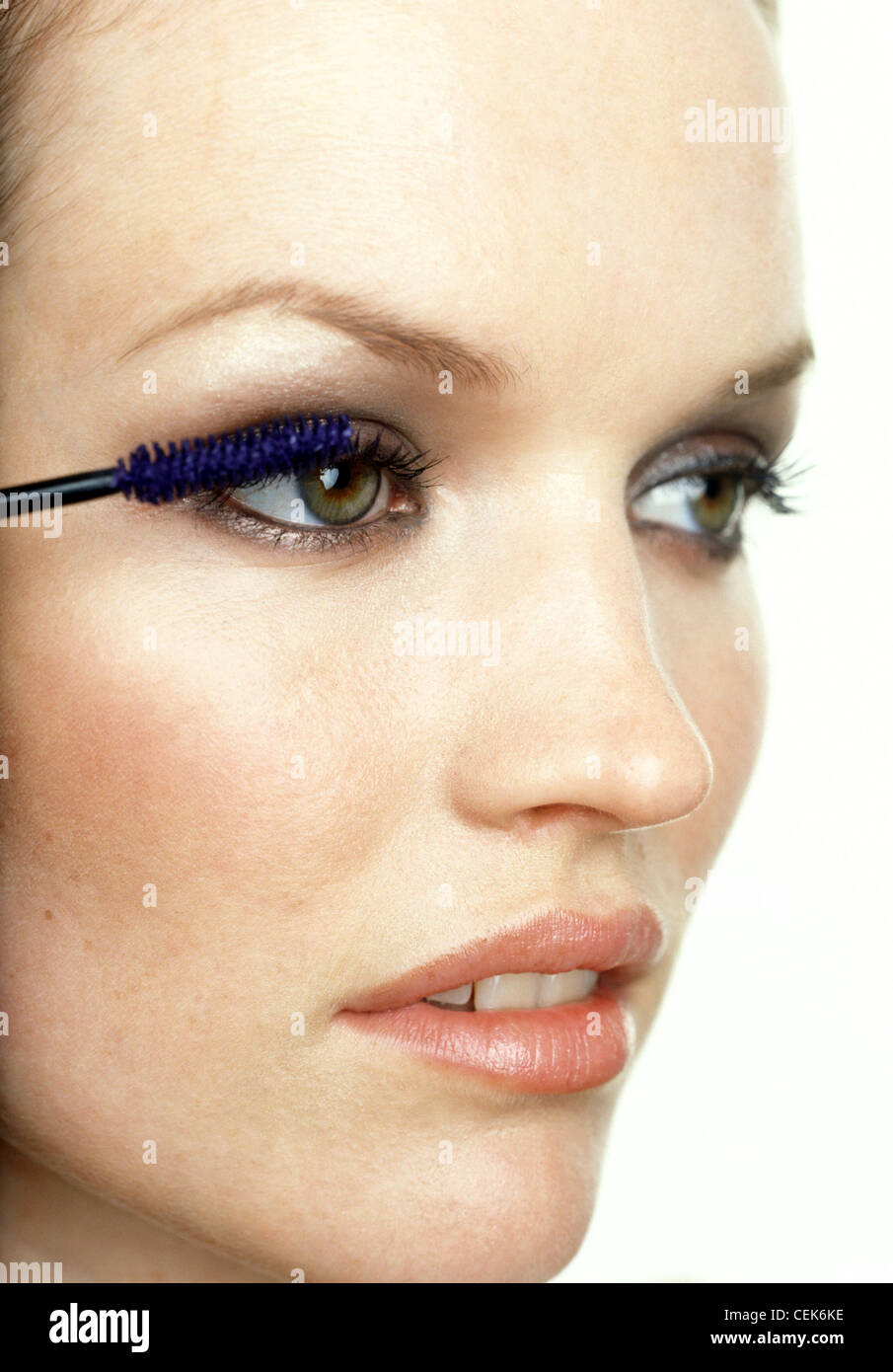 Close up image of female's face, applying purple mascara, unsmiling ...