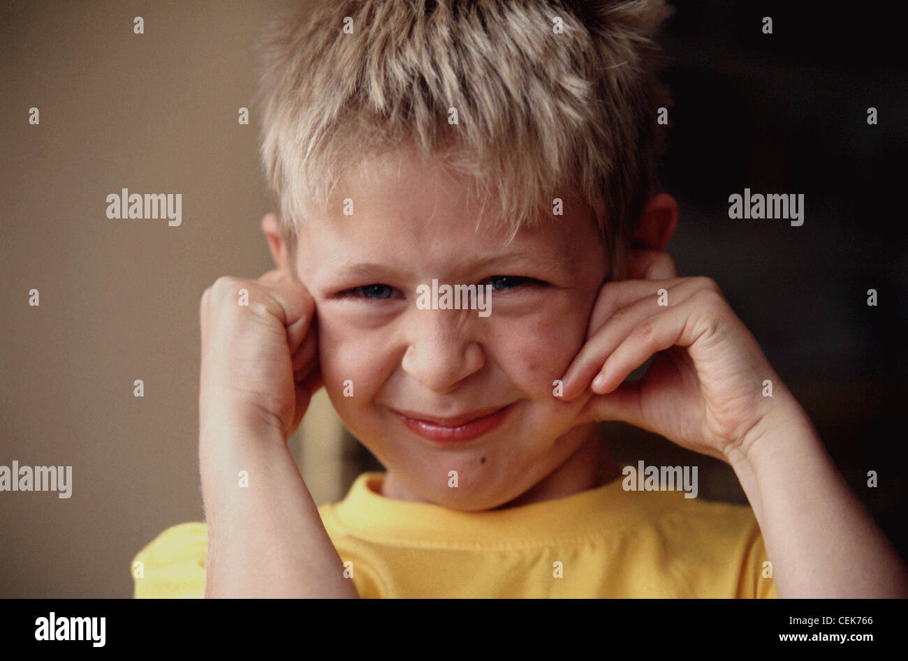 Male child blonde spiky hair wearing yellow t shirt pulling face ...