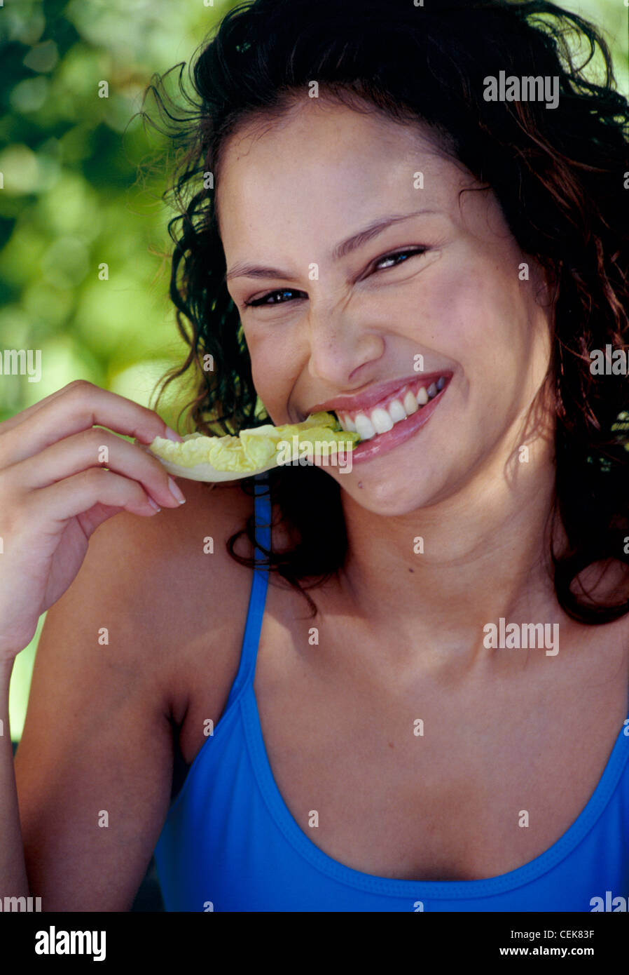 Female Long Curly Brunette Hair Wearing Blue Vest Top Eating Lettuce