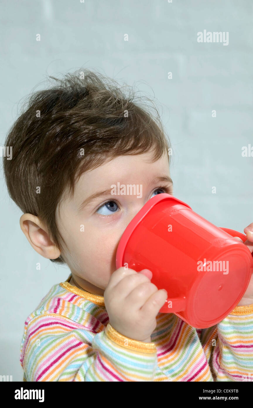 Female child wearing multicoloured striped top drinking from red beaker ...