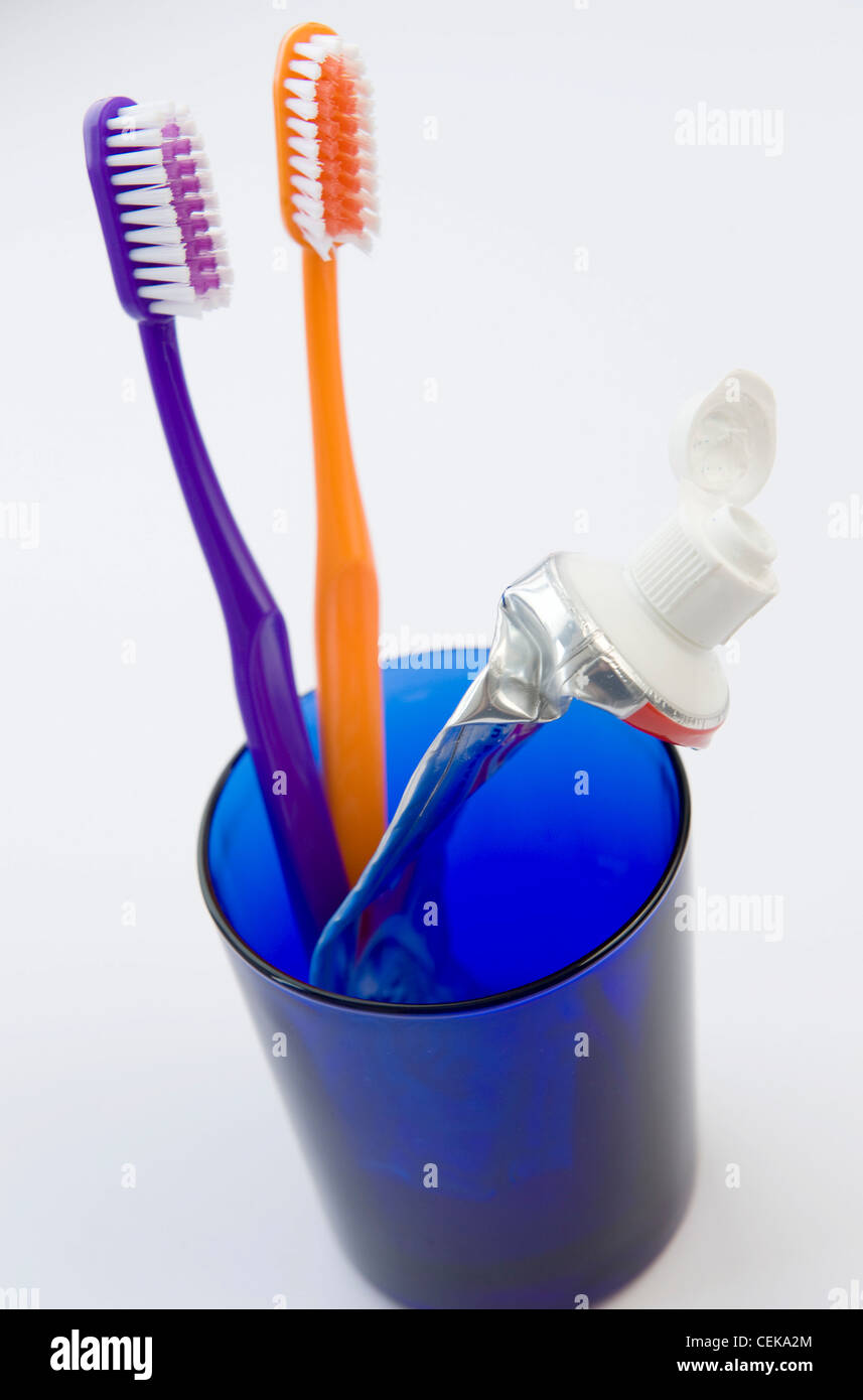 A blue glass with a used tube of toothpaste, a purple toothbrush and ...