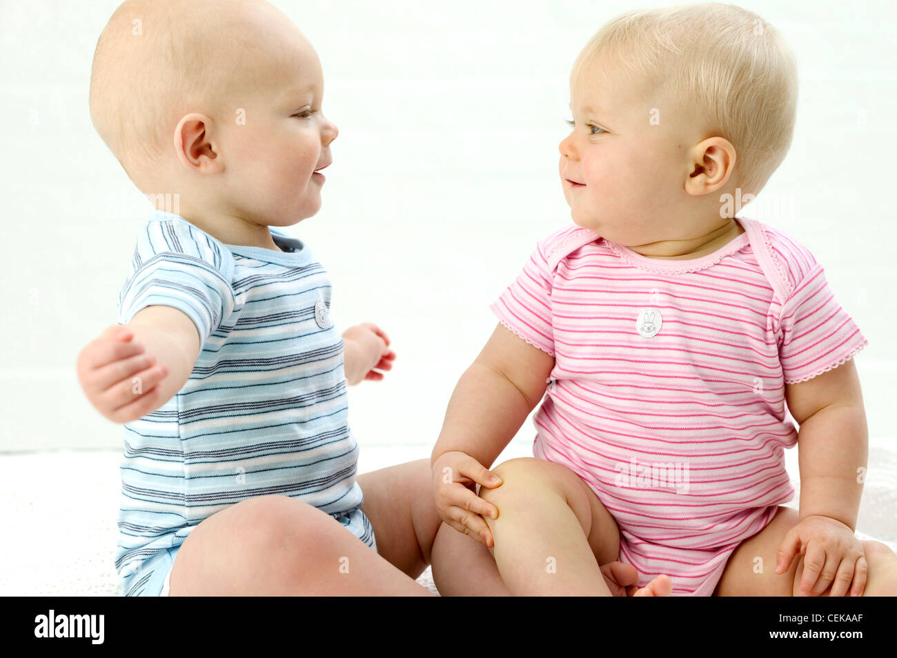 Two babies looking at each other smiling, male baby on left wearing ...