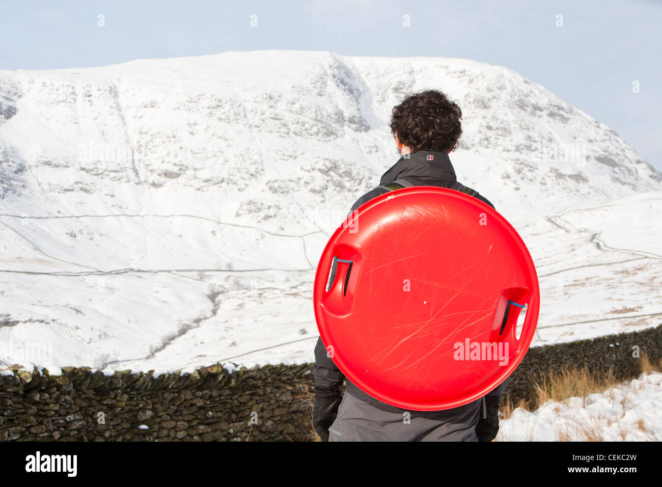 A man with a plastic sledge in the snow on Wansfell above Ambleside in ...