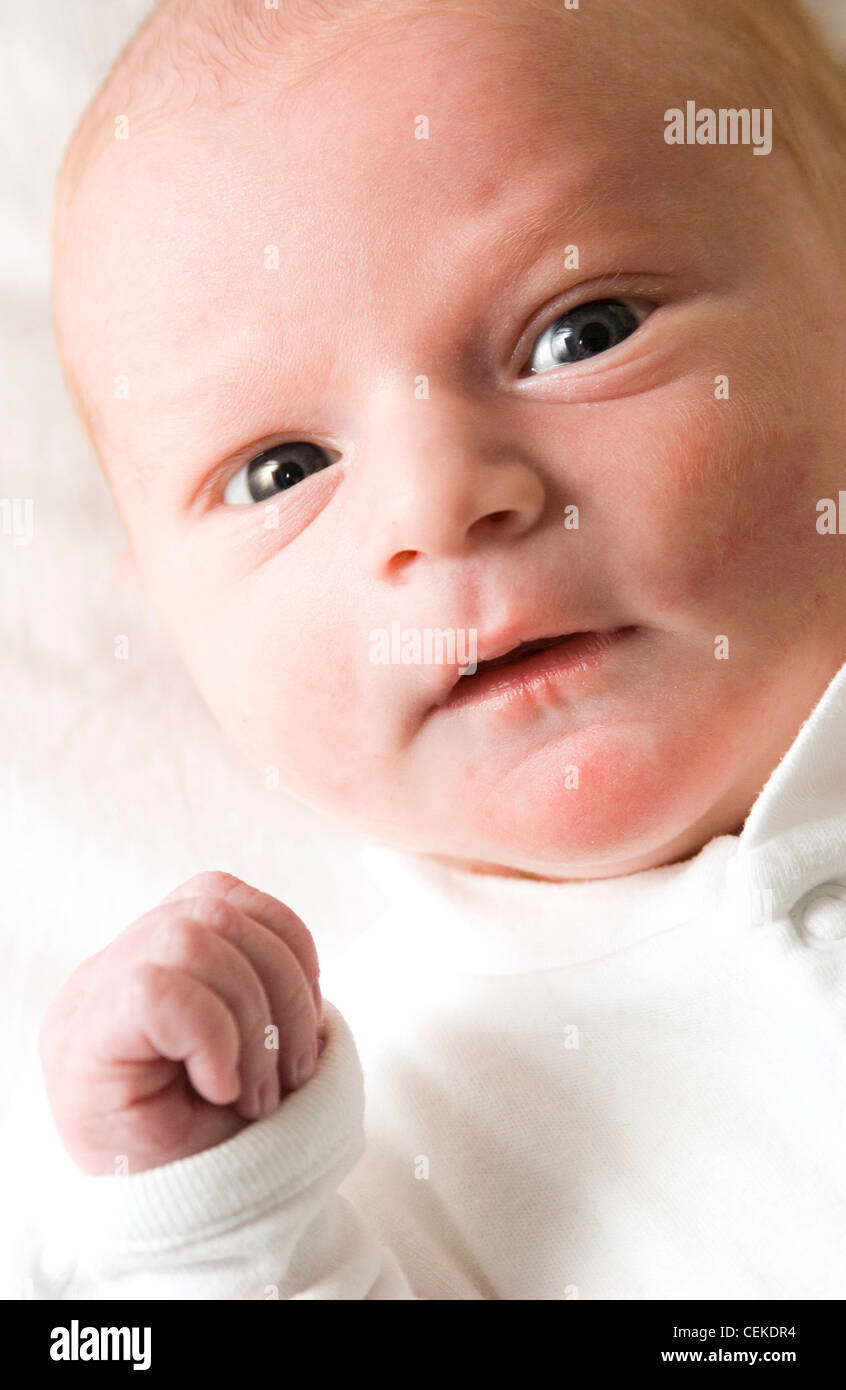 New born baby wearing white baby gro looking past camera unsmiling ...