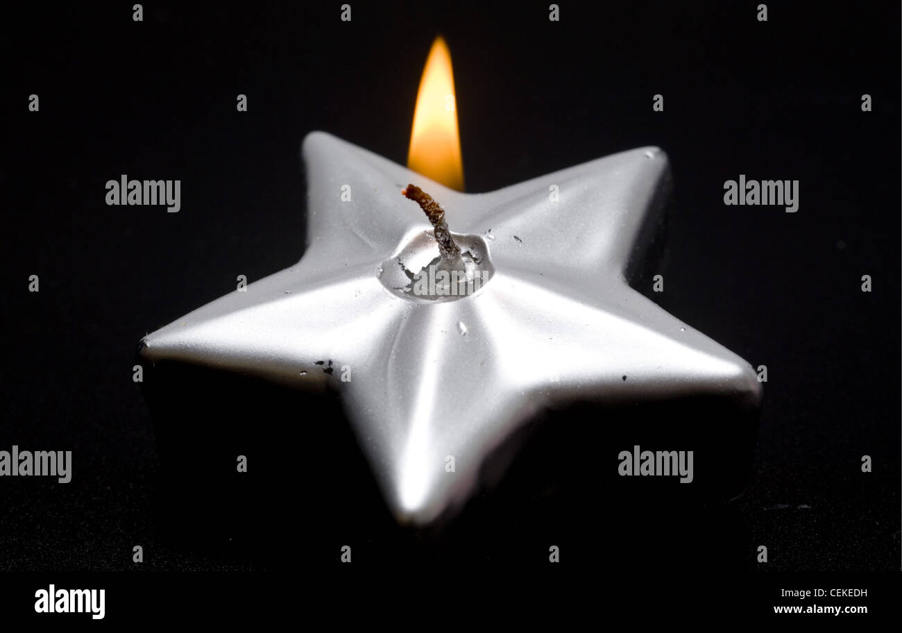 Burning metallic Christmas star candle, pictured on black surface Stock ...