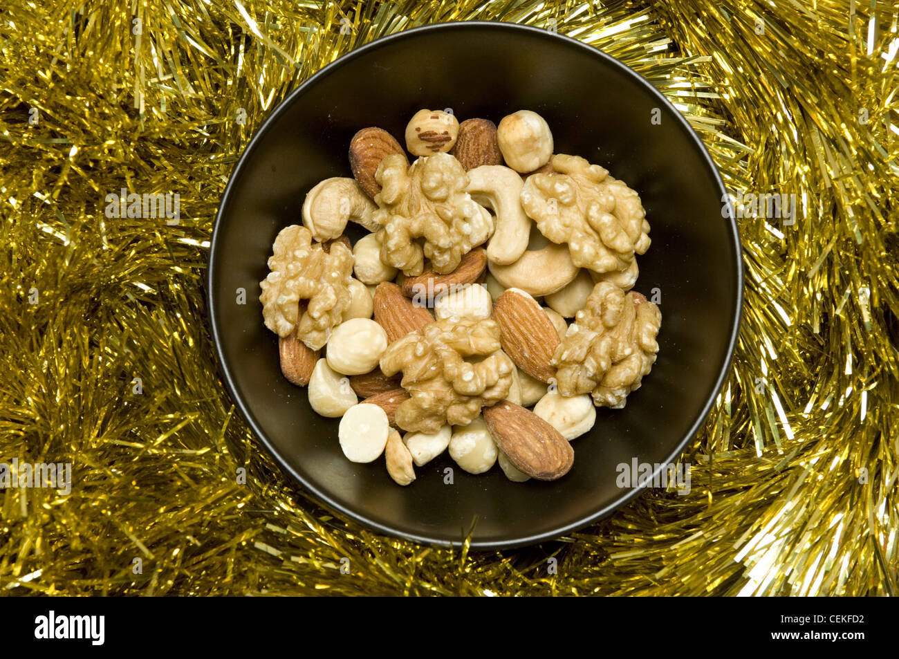 Aerial of mixed nuts in a dark ceramic bowl, resting on gold Christmas ...