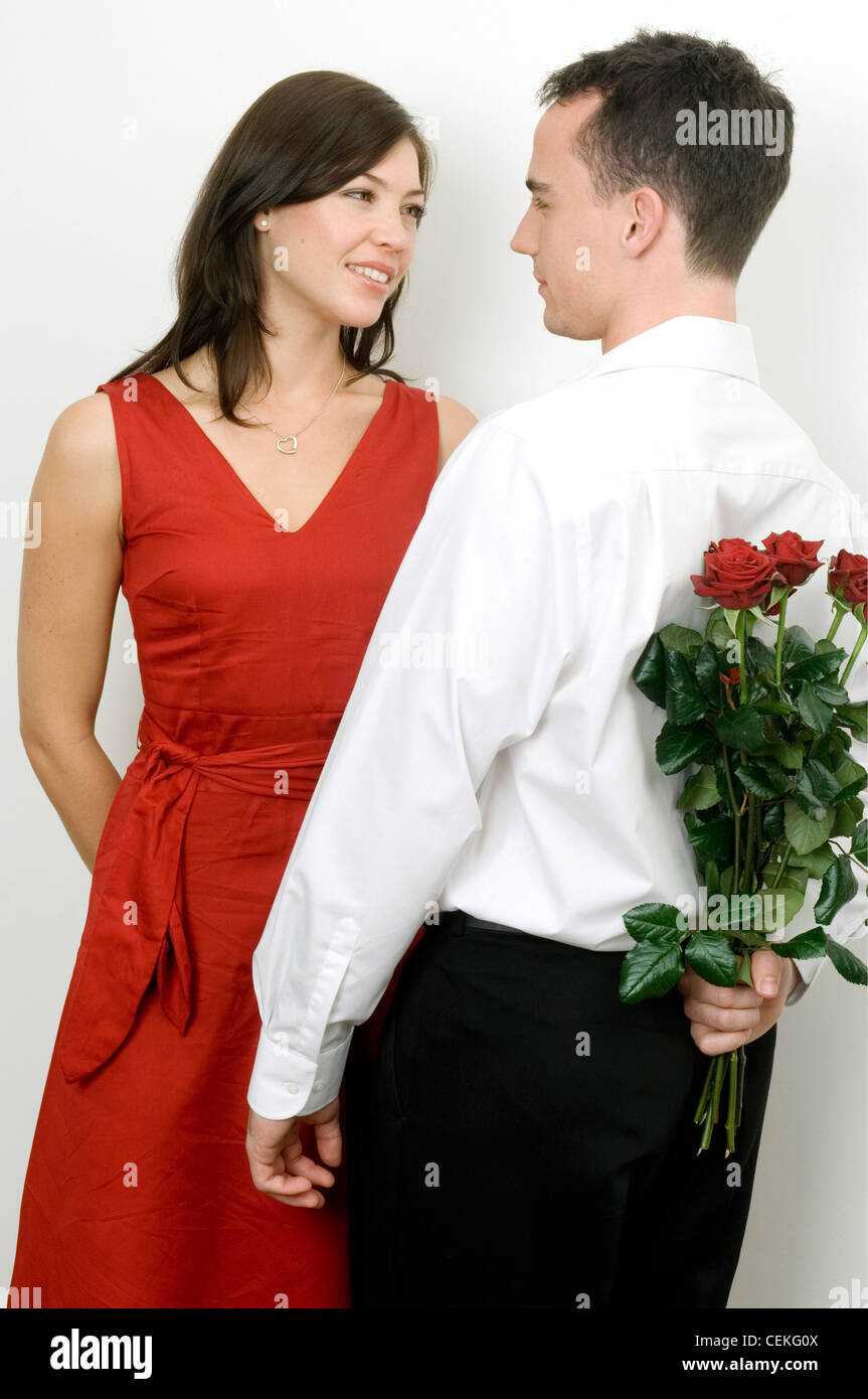 Brunette male wearing a white shirt holding a bunch of red roses behind ...