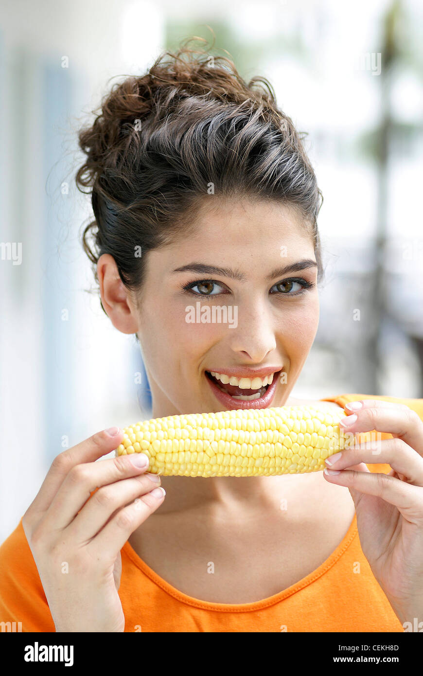 Female with long brunette wavy hair worn tied up wearing orange top ...