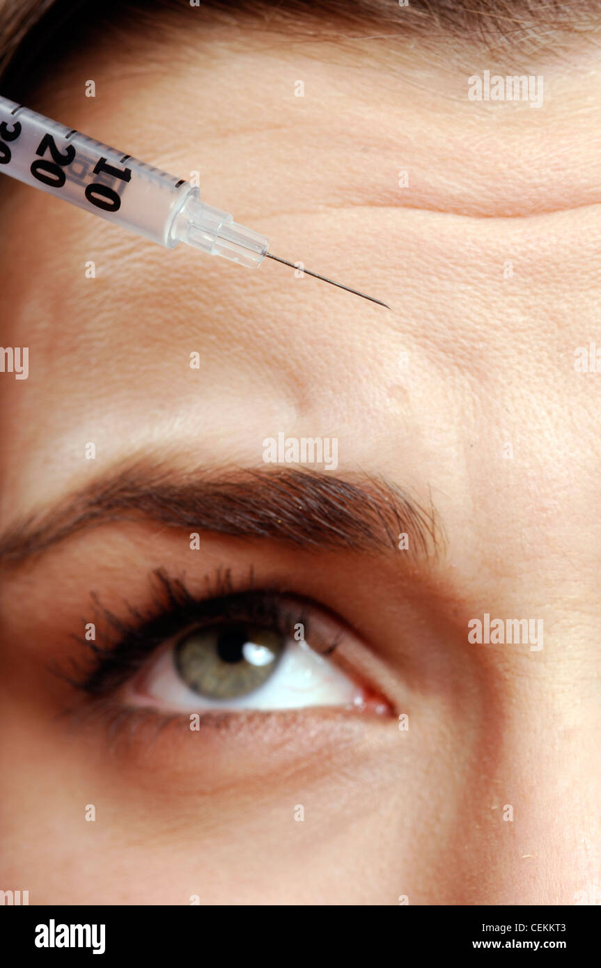 Close up of female forehead and eye with syringe needle held to ...