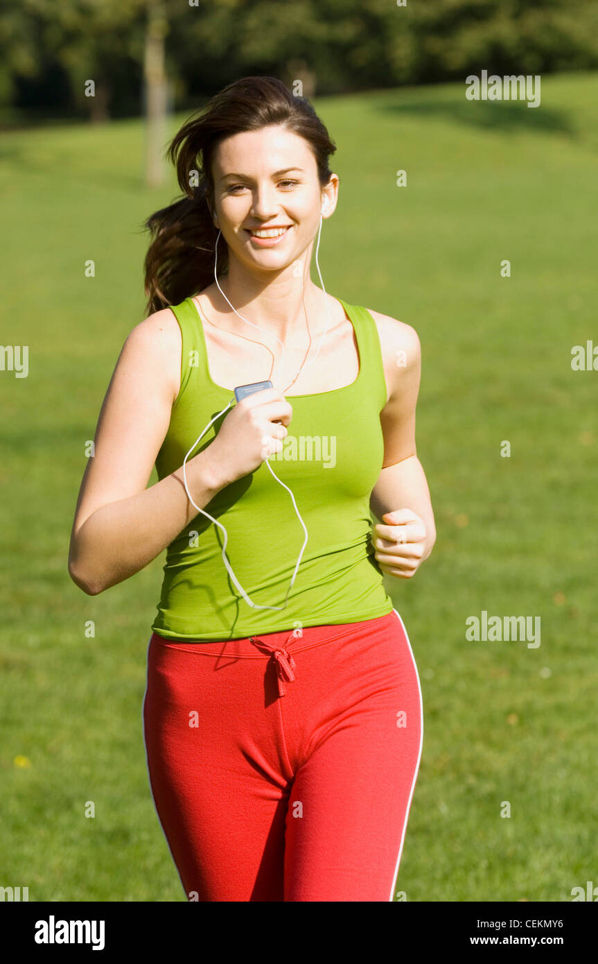 Female wearing red trousers, green vest top and white trainers running ...