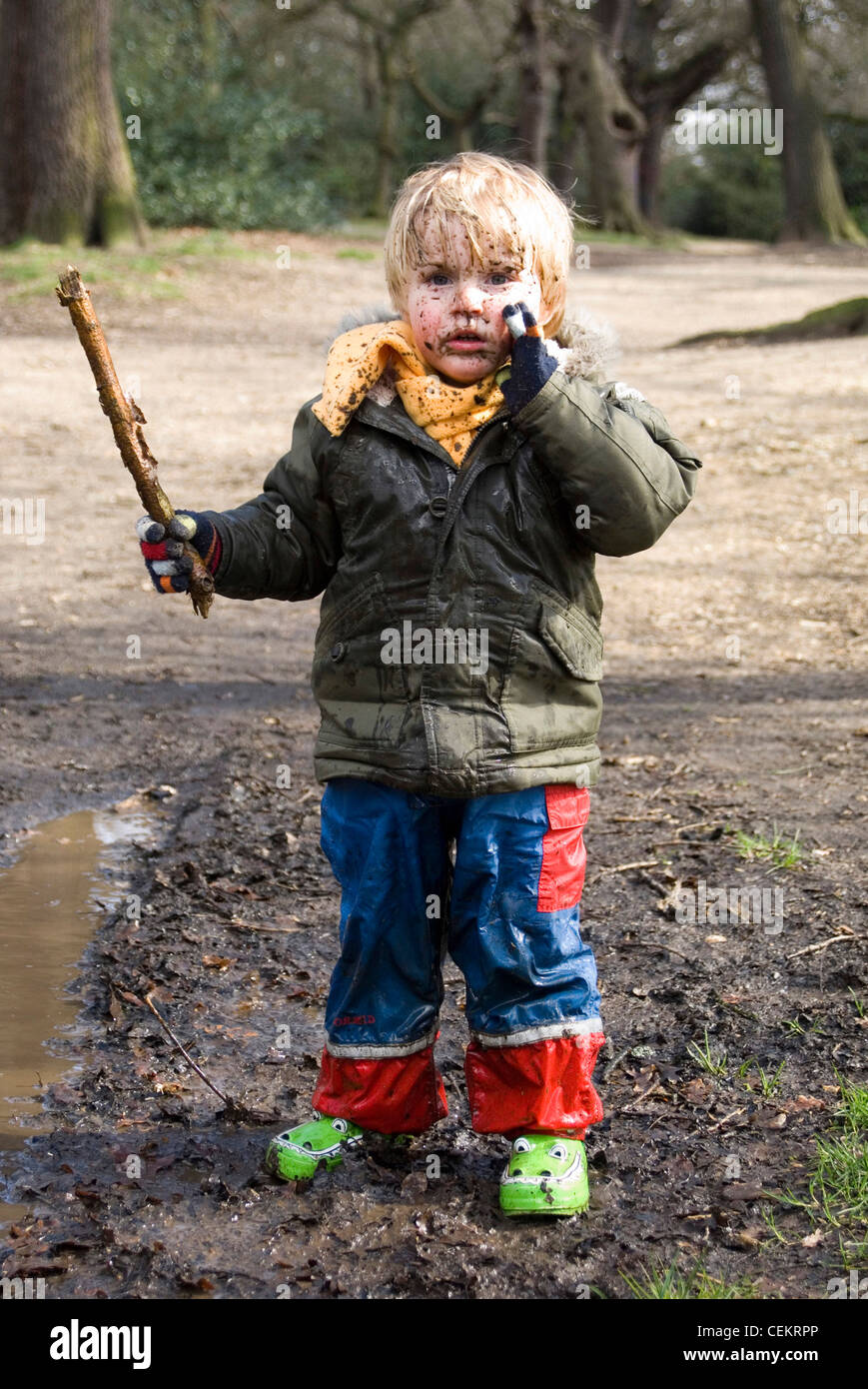 A male child standing by a large muddy puddle with mud splattered over ...