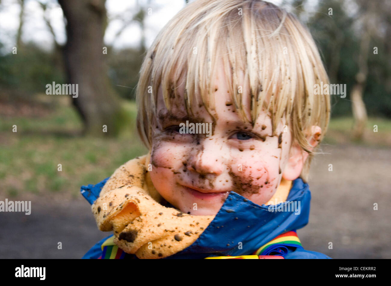 A male child standing by a large muddy puddle with mud splattered over ...