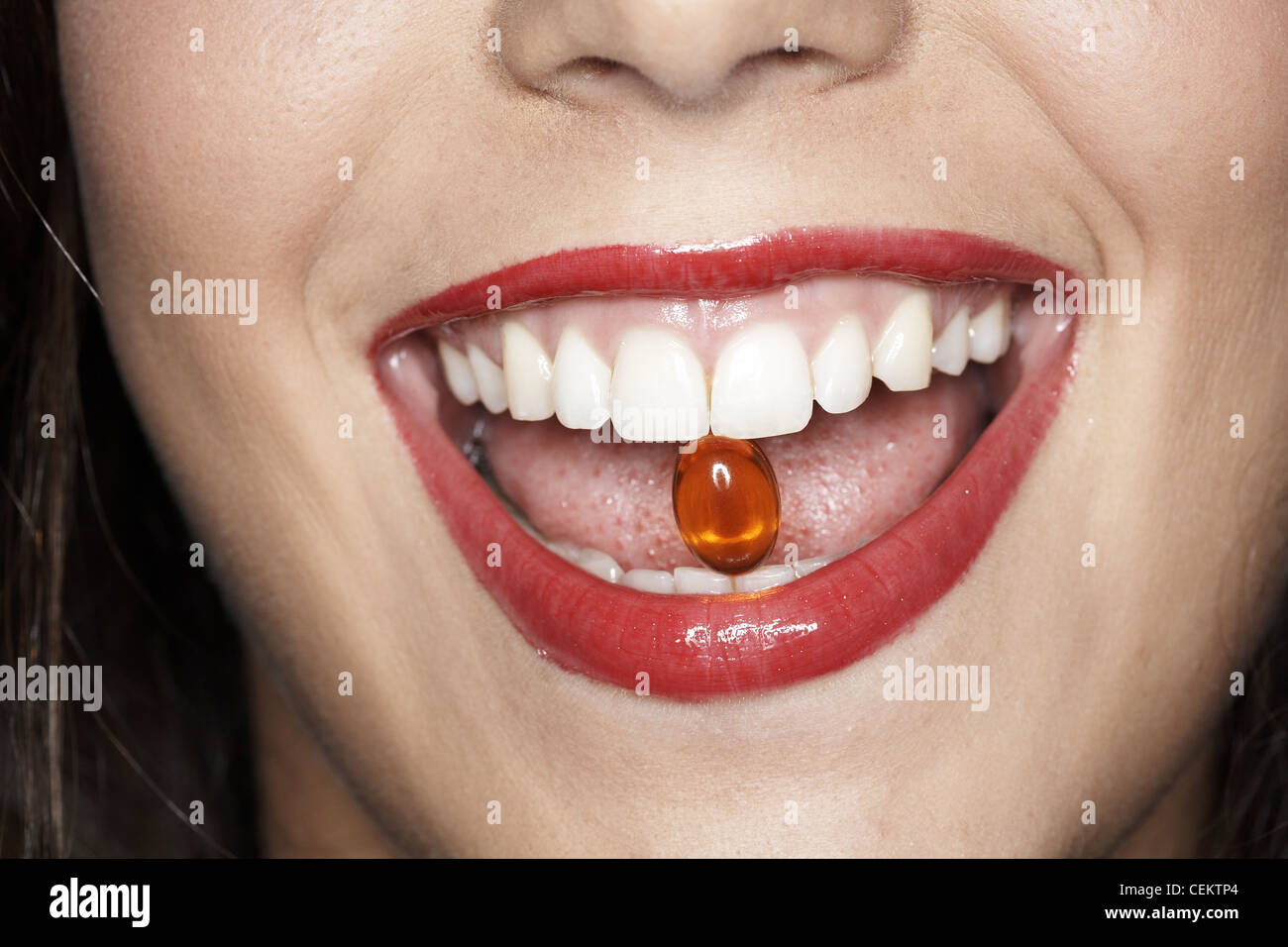 Female wearing bright red lipstick with a supplement capsule between ...