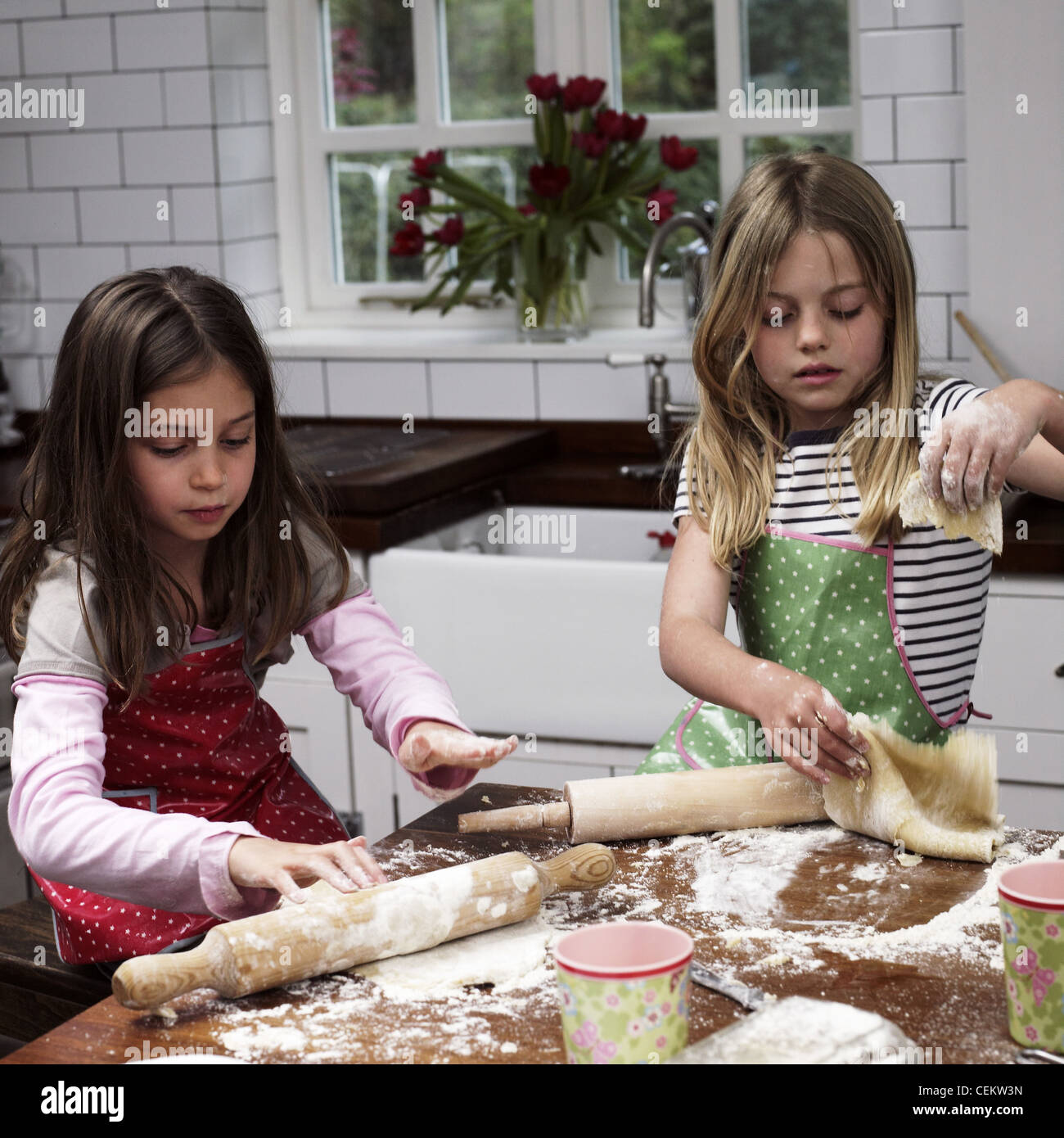 Two young girls with rolling pins, rolling out mixturebiscuits Stock ...