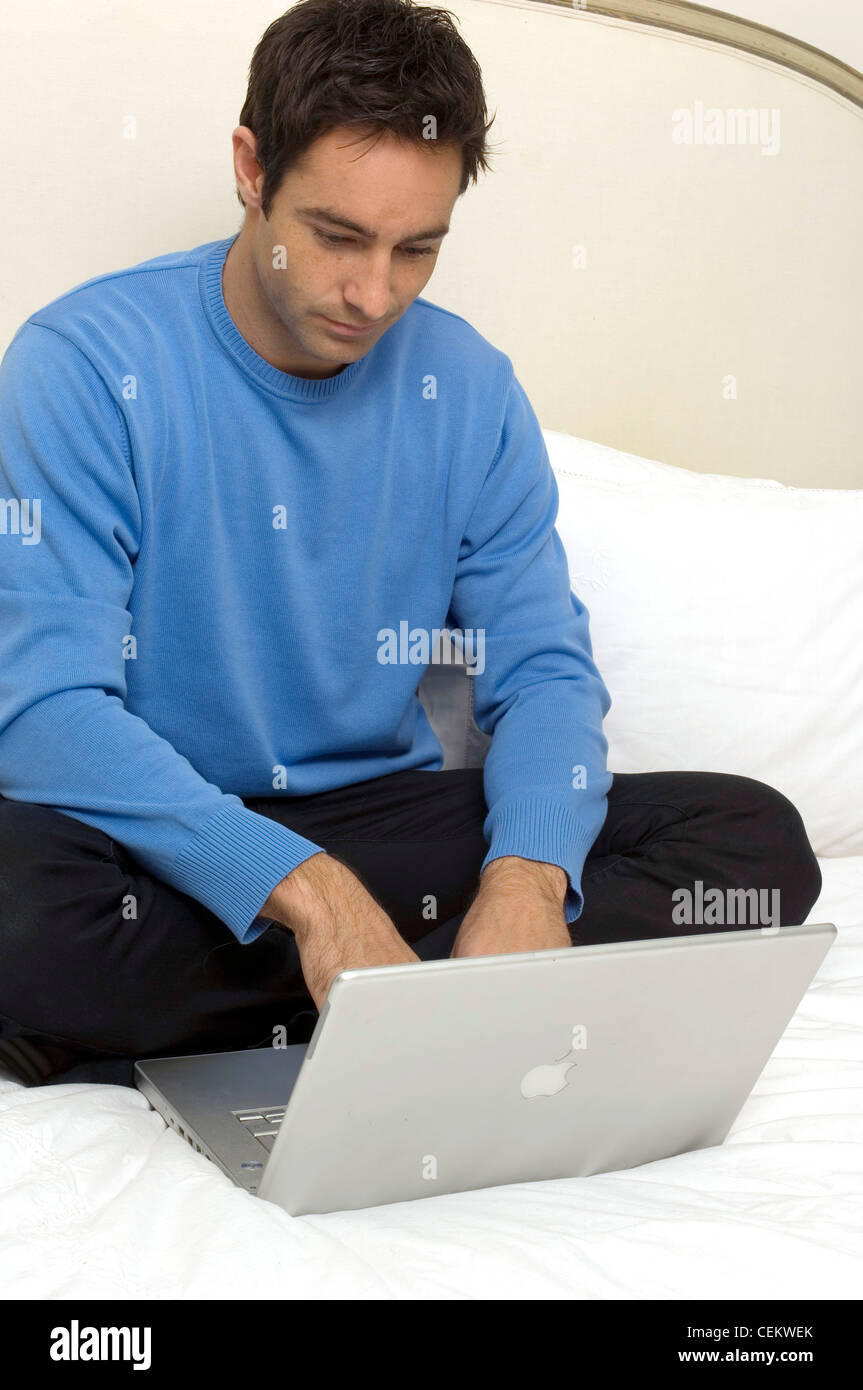 Male sitting with legs crossed on a bed using a laptop computer Stock ...