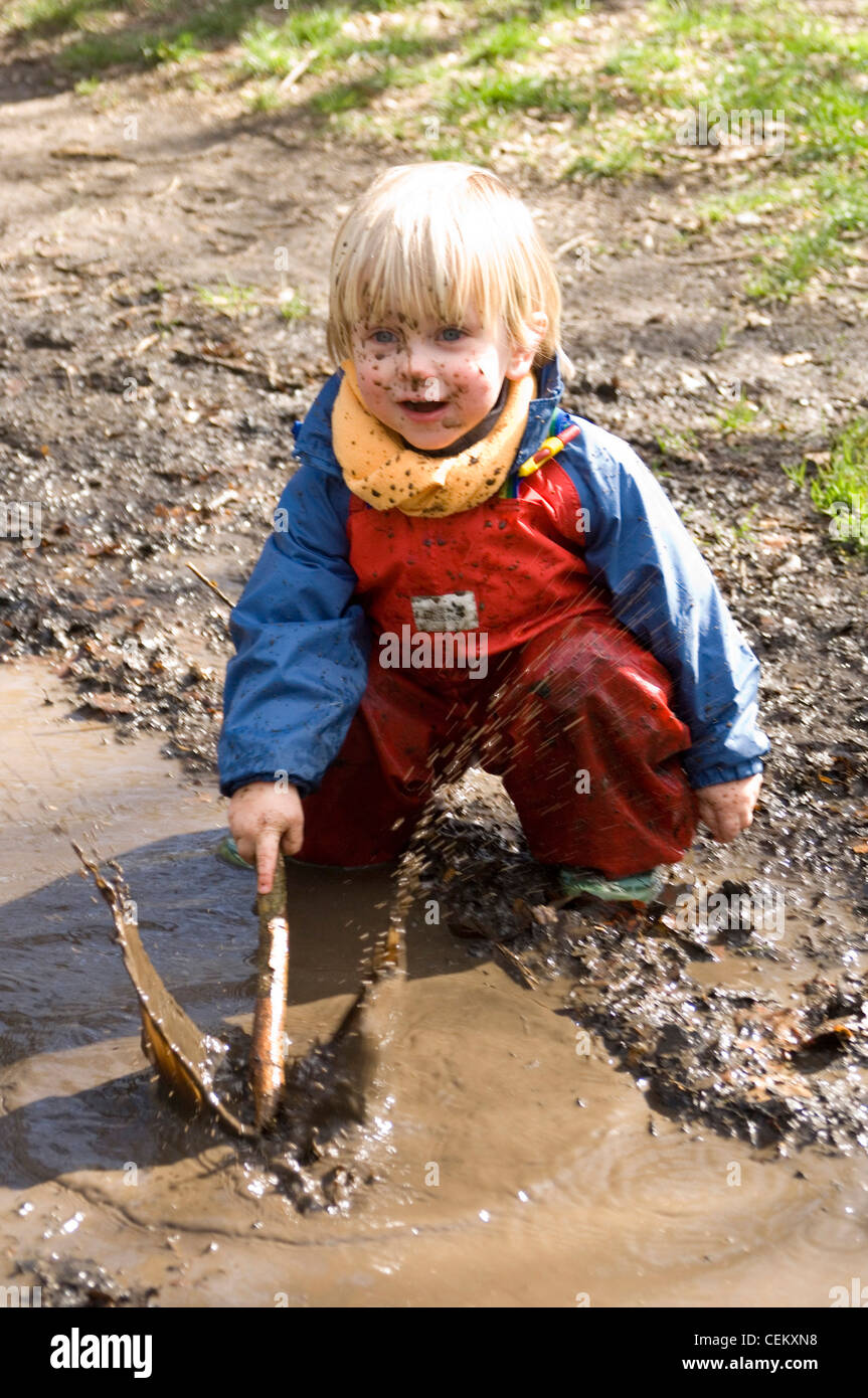 A male child standing by a large muddy puddle with mud splattered over ...