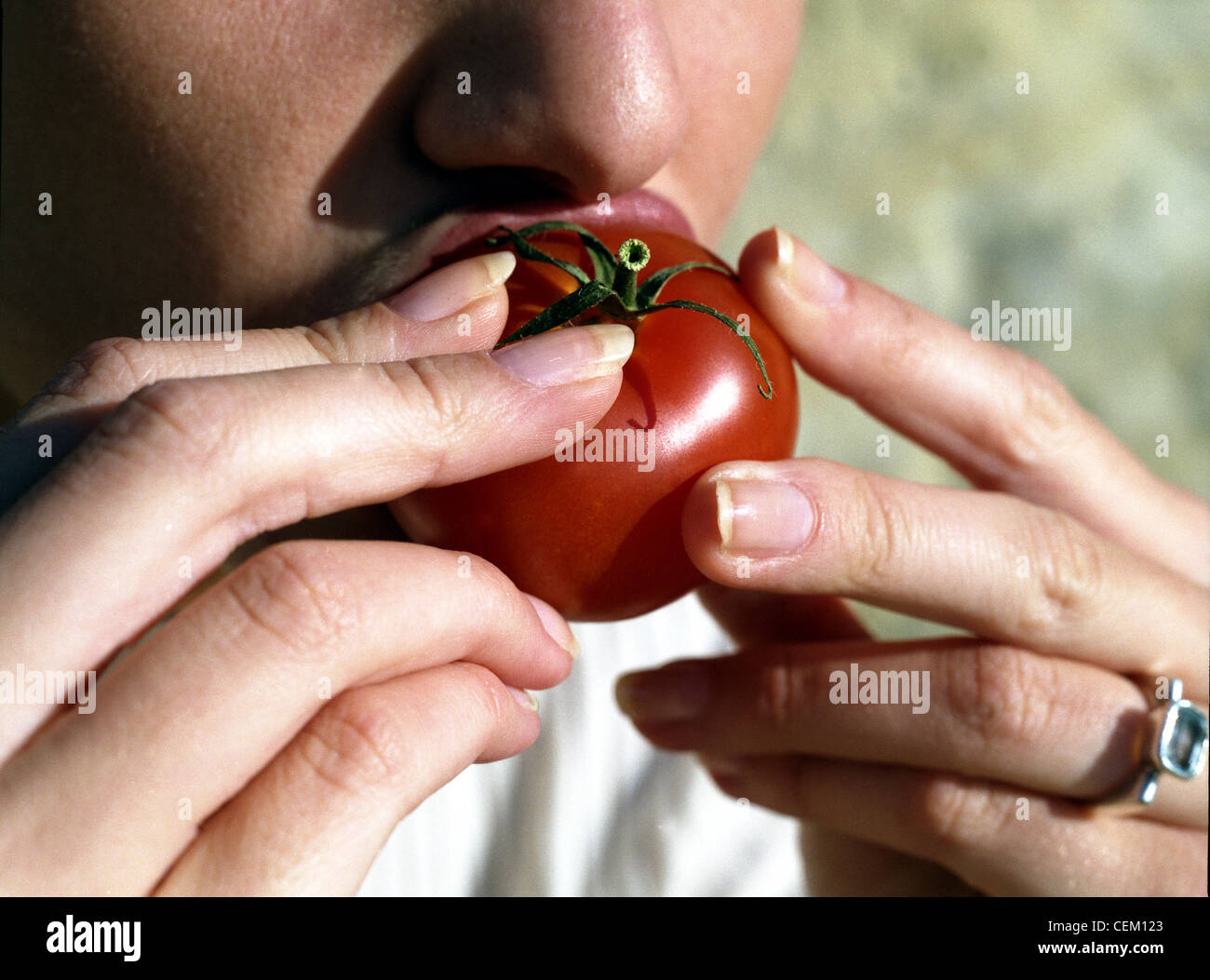 A female holding a red tomato, biting into it, with some large rocks in ...