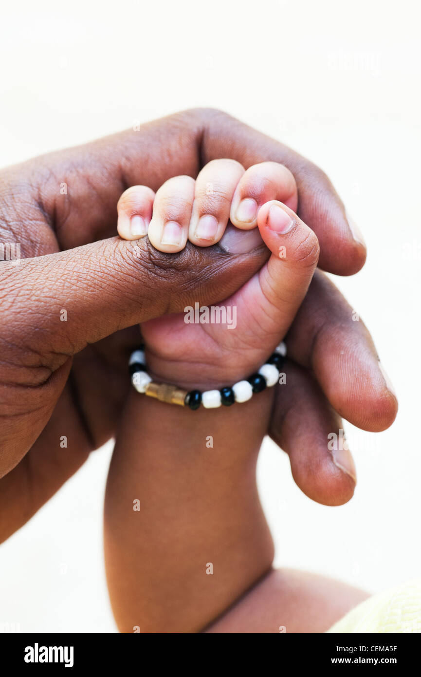 Indian mans hand holding his new born babies hand against a white ...
