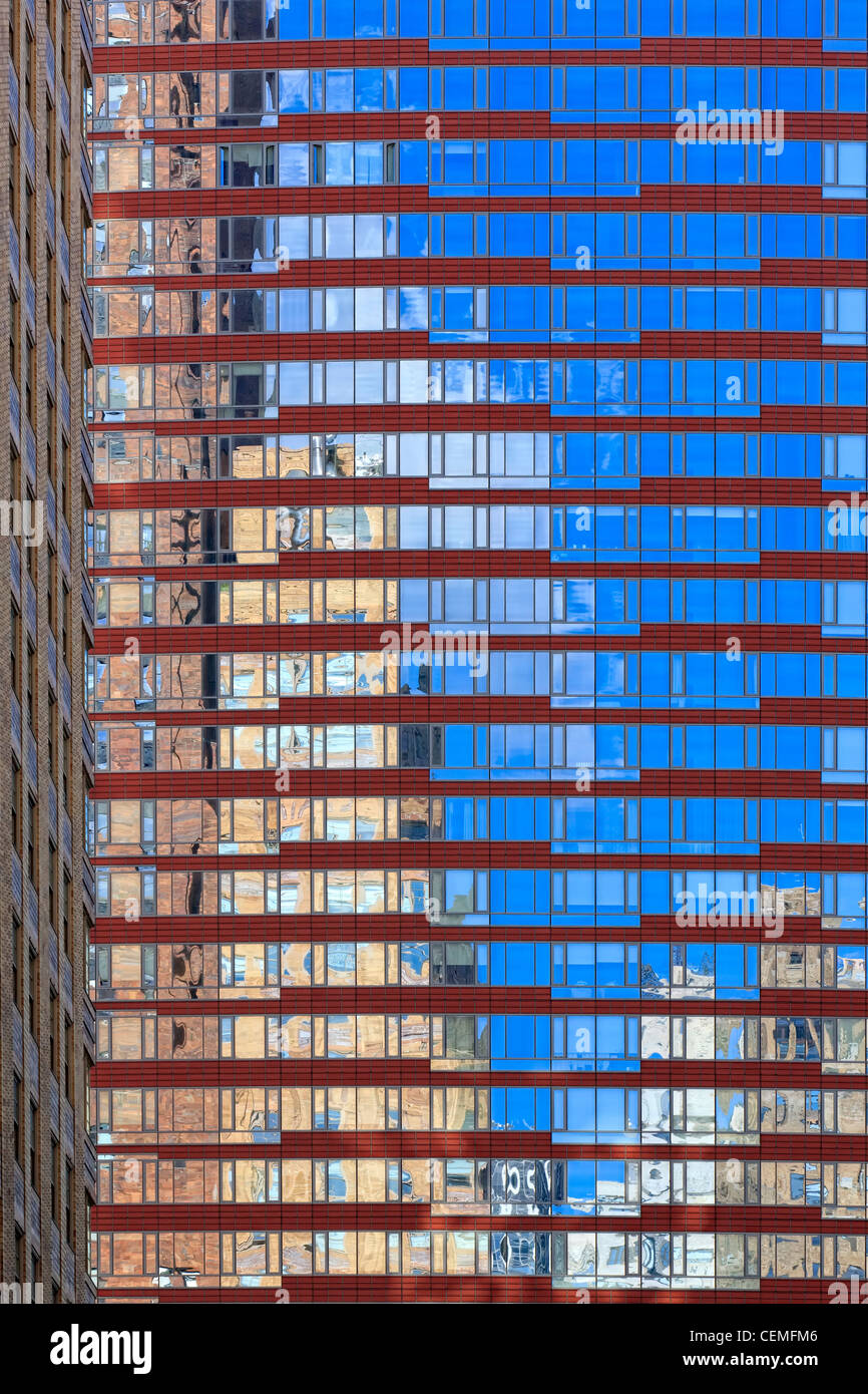 A modern glass-box high rise building with blue sky and other building ...