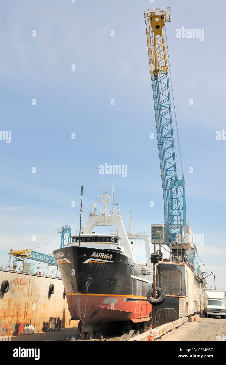 A large ship in dry dock, with a crane attached to dry dock in image ...