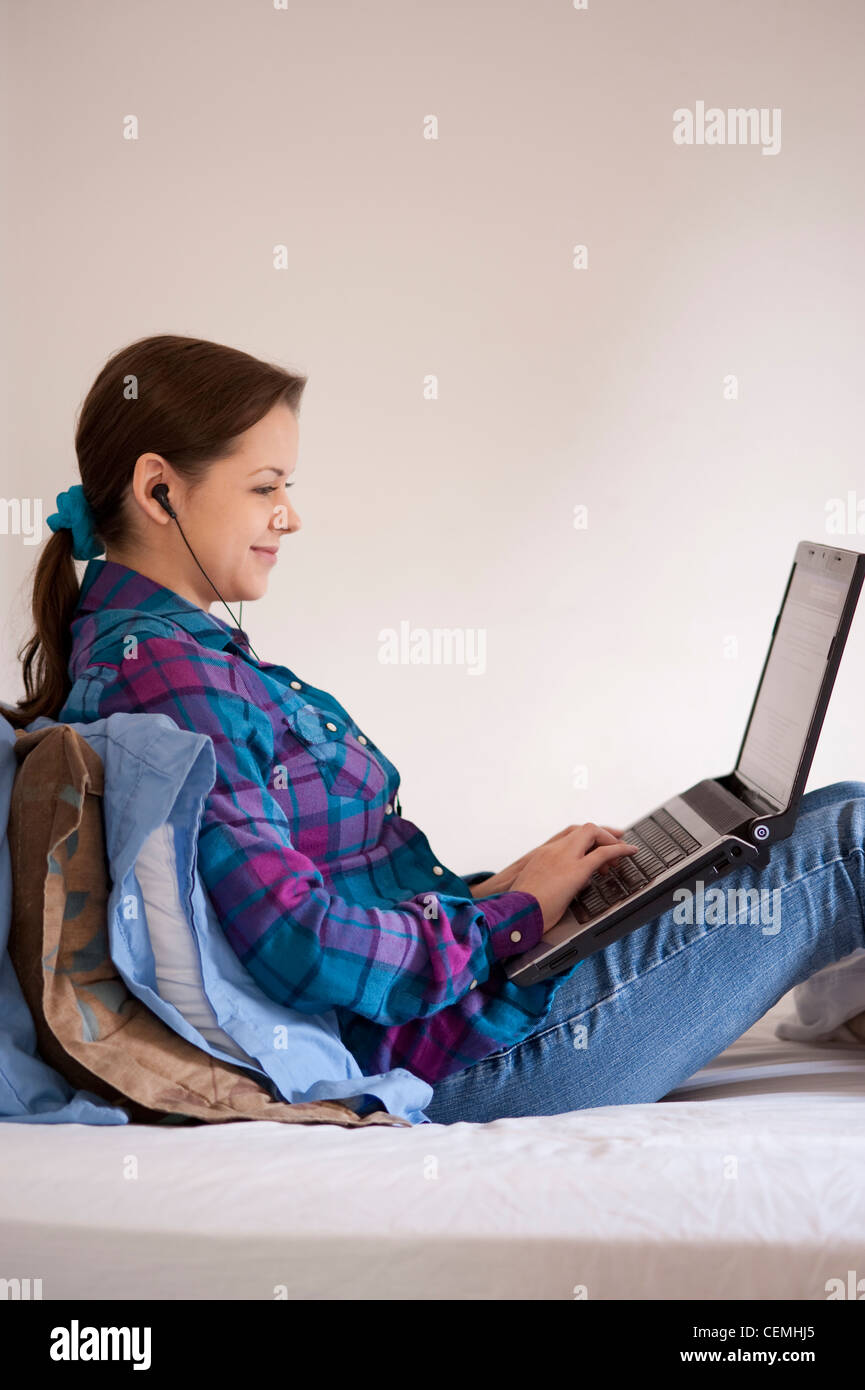 College student sitting on bed using a laptop in dorm room before ...