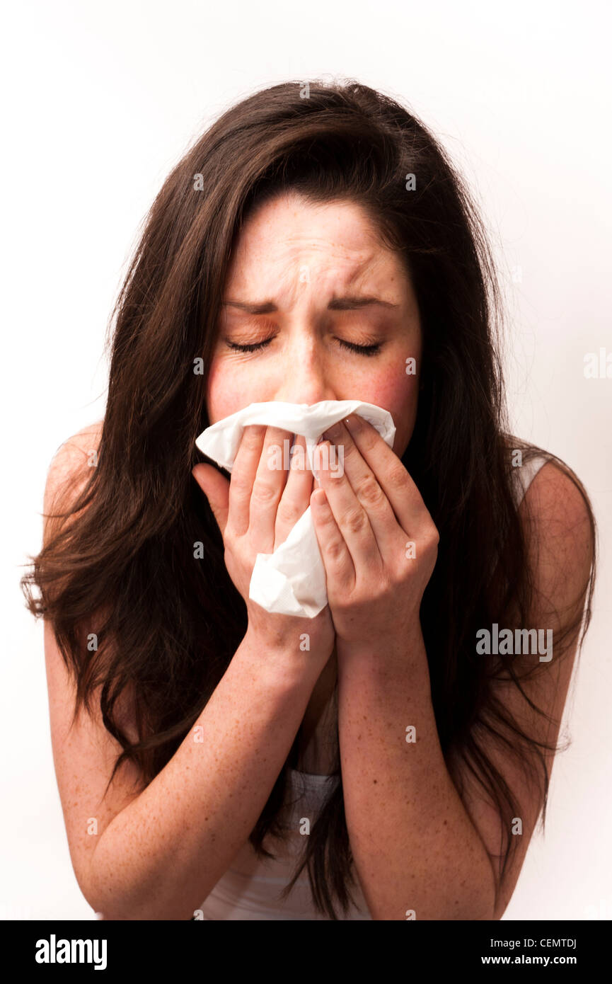 A young woman with brown hair and eyes feeling ill sneezing blowing her ...