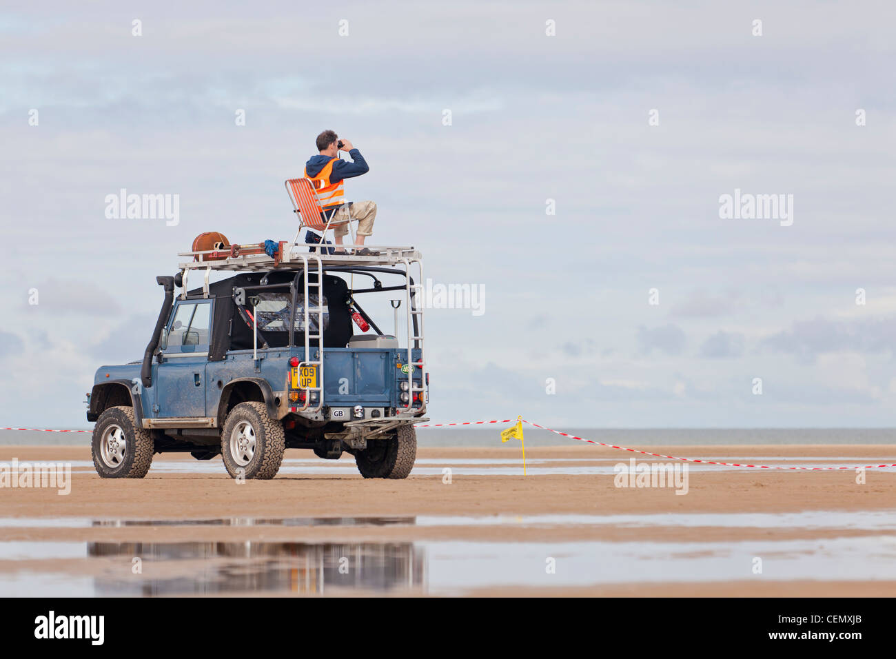 a landrover (land rover) on a vast beach with two people sitting on top ...