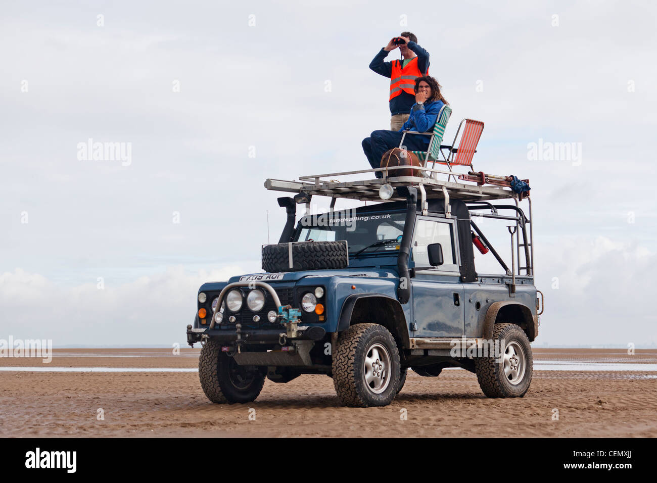 a landrover (land rover) on a vast beach with two people sitting on top ...