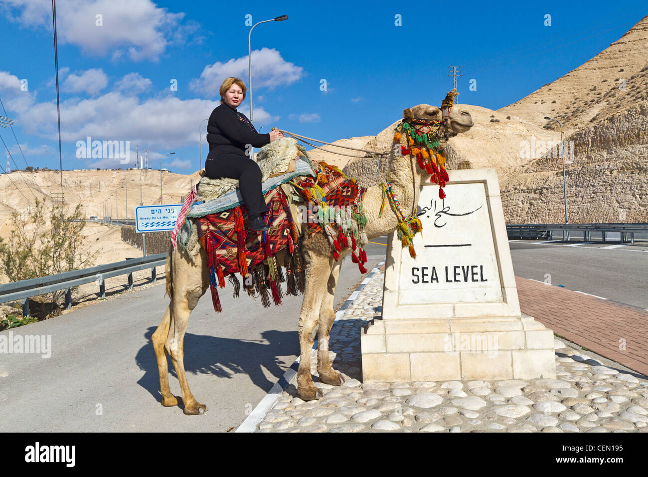 Tourist rides a camel at the "Sea Level" marker on Highway 1, the road ...