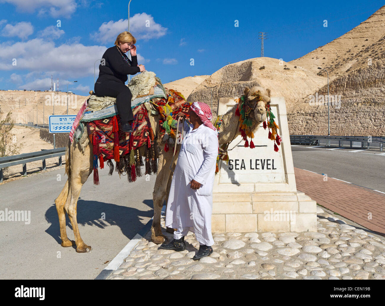 Tourist rides a camel at the "Sea Level" marker on Highway 1, the road ...