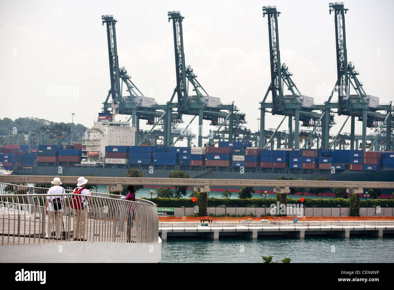 Tourists look out over Sentosa island as a container ship lies docked ...