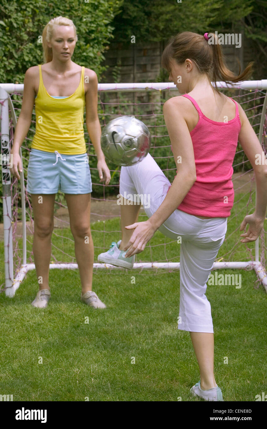 Two females playing football in garden, back view of female on right ...