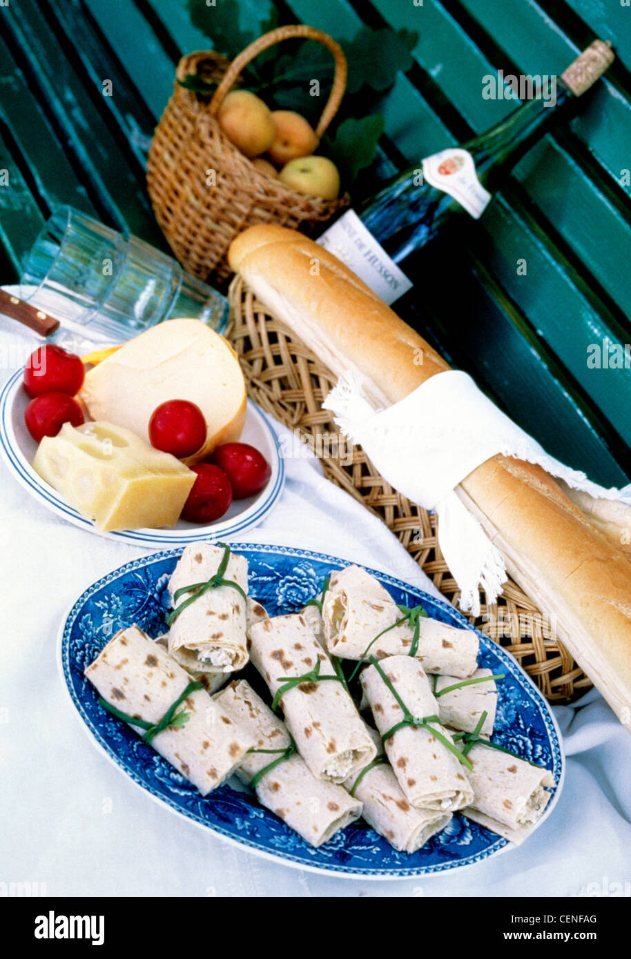 Picnic on green wooden bench, French bread, basket of apples, bottle of ...