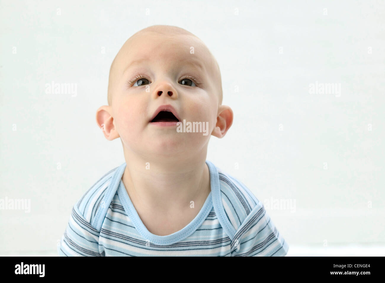 Male baby wearing blue striped top, looking up with mouth open smiling ...