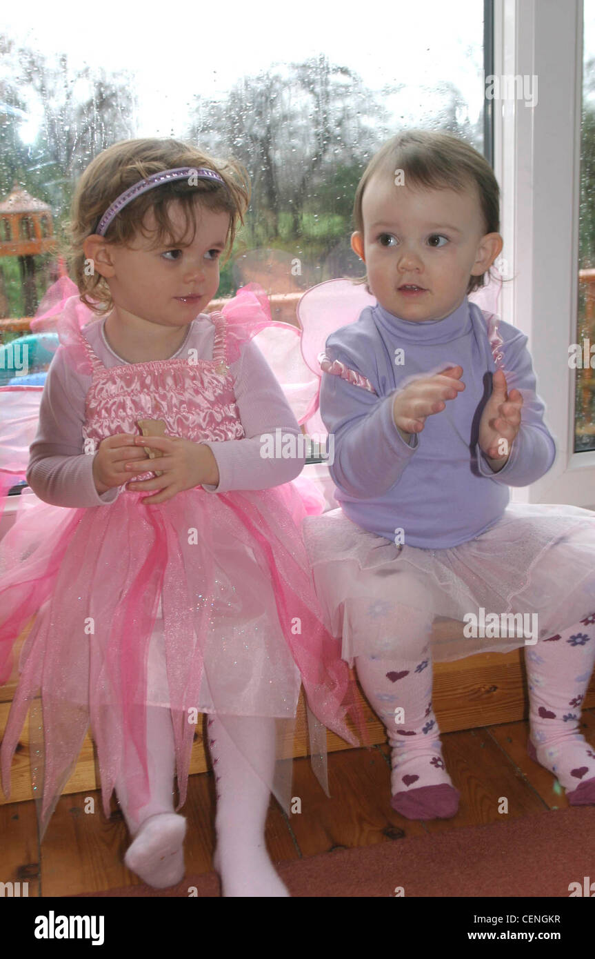 Two female children wearing fairy costumes with wings sitting by window ...