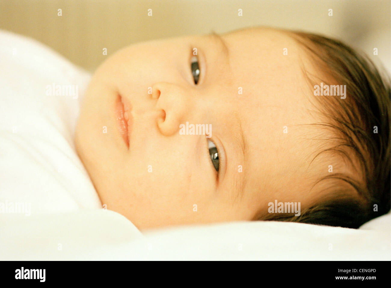 Baby with dark brown hair in pink babygro lying on back with face ...