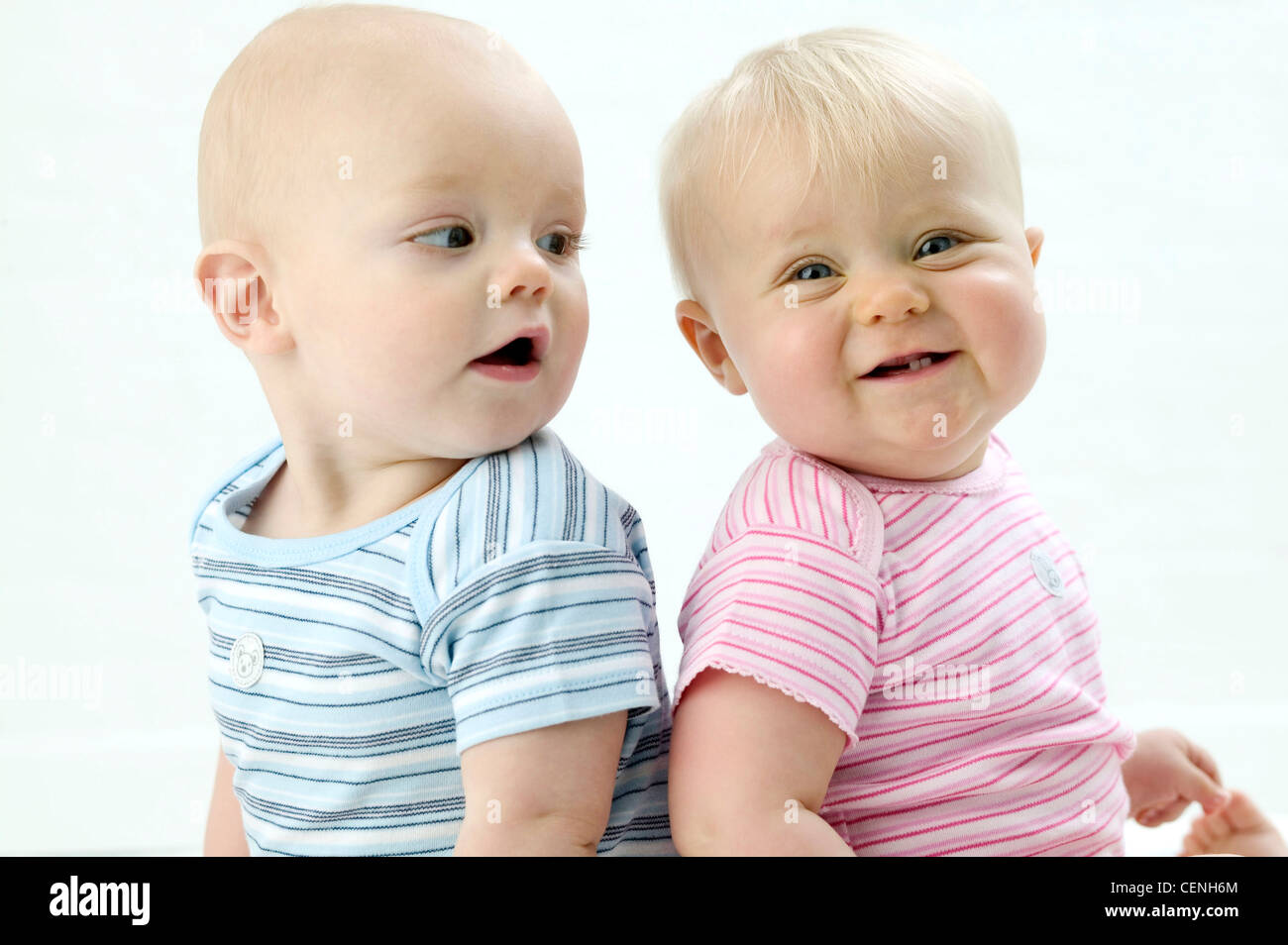 Two babies sitting back to back, male baby on left wearing blue striped ...