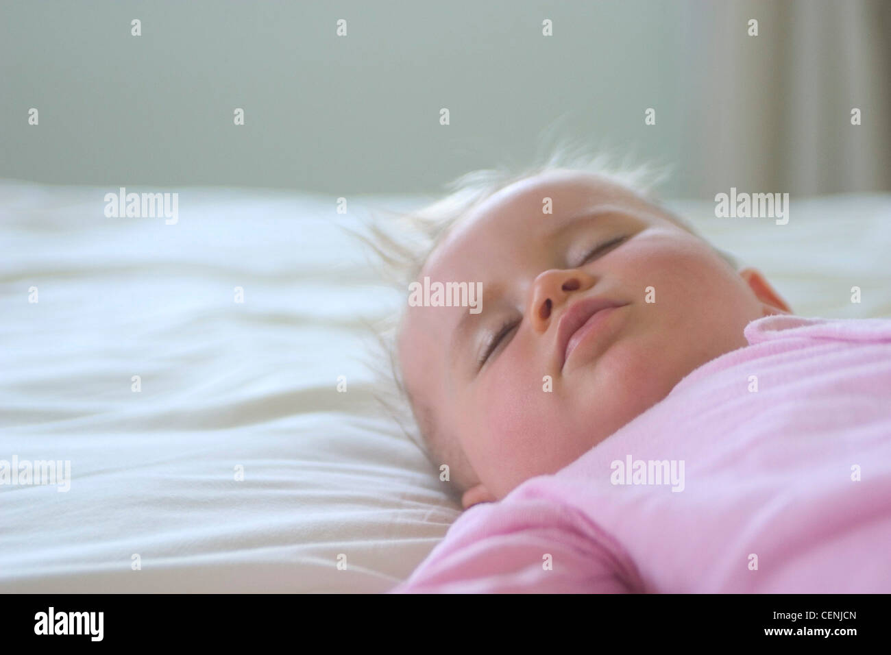 Baby wearing pink babygro, lying on back on bed with eyes shut asleep ...