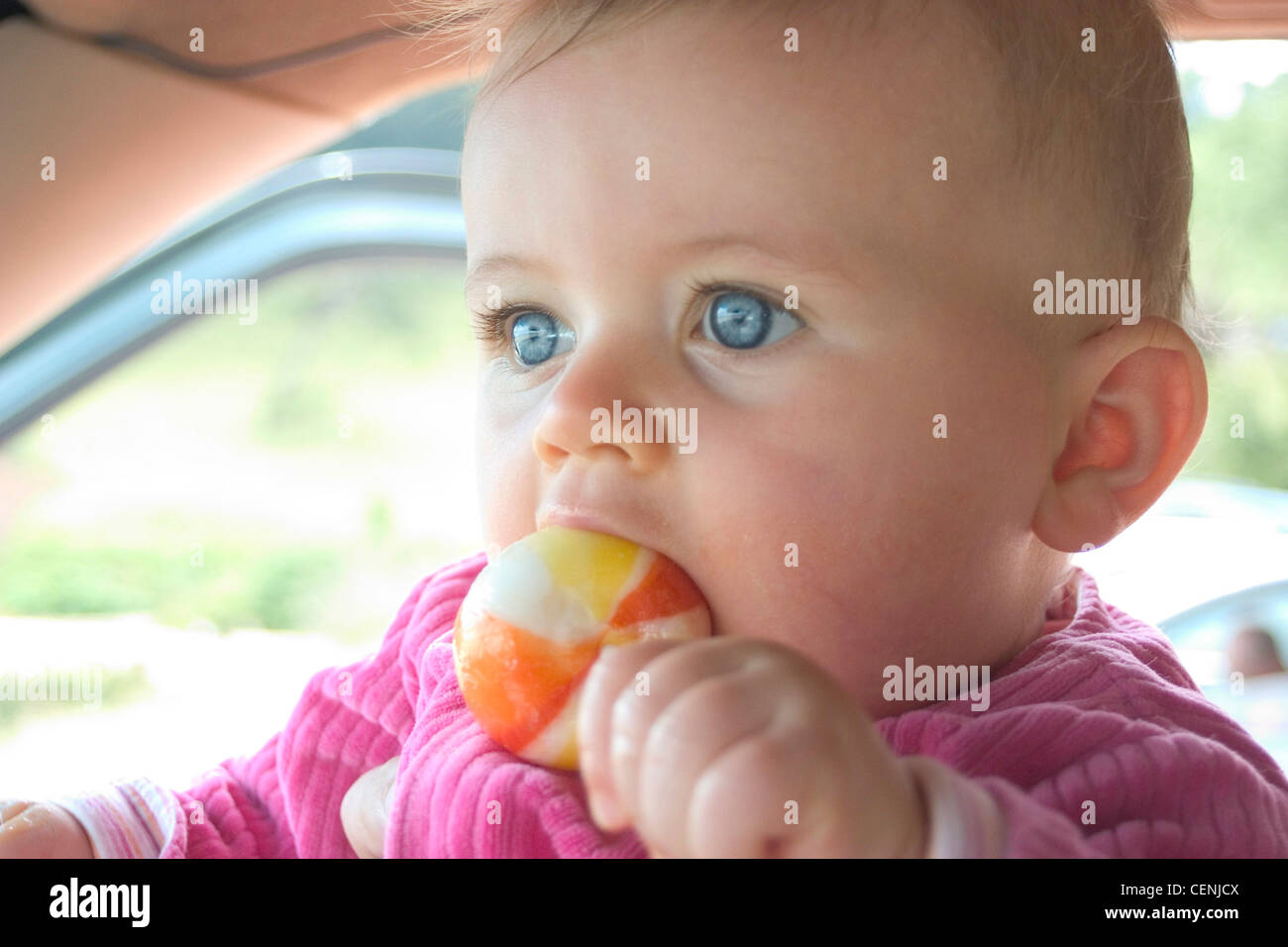 Baby in car wearing pink top, with large lollipop in mouth looking to ...