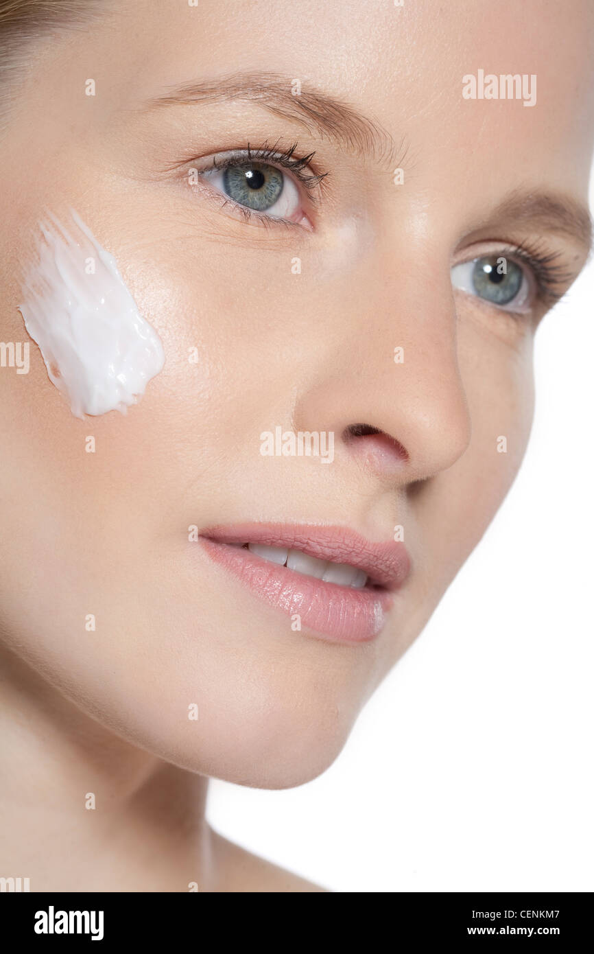 Female wearing subtle make up, applying face cream to her cheekbone ...
